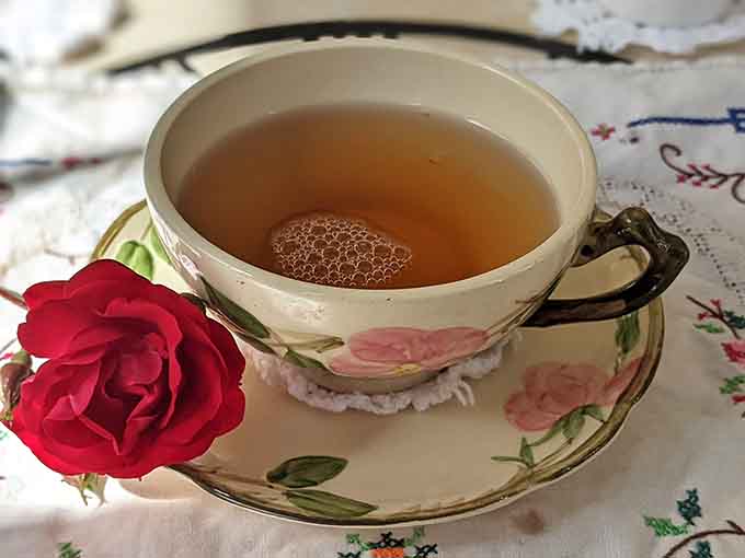 Delicate vintage teacup cradles hot tea beside a fresh rose, making every sip feel like attending the world's loveliest party.