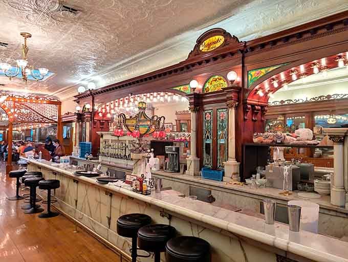 That ornate soda fountain counter gleams like a jewel, ready to dispense phosphates and dreams in equal carbonated measure.