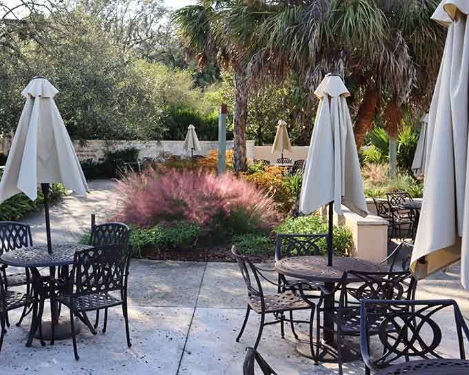 Dappled sunlight filters through palms onto wrought-iron tables in this secret garden where nature provides the perfect ambiance.