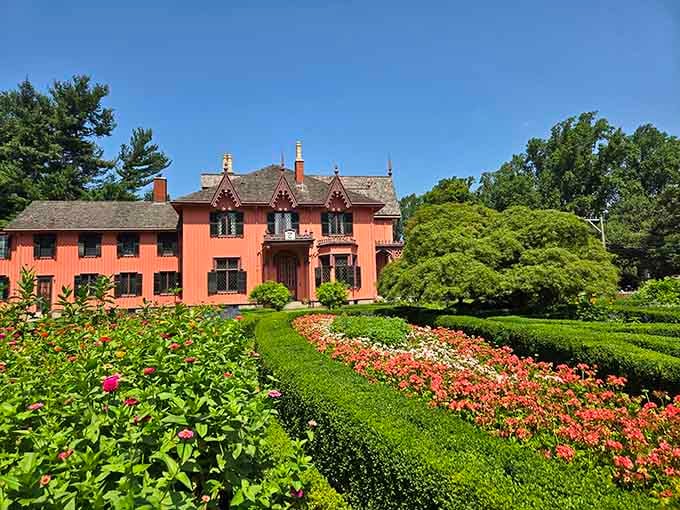 The coral-pink cottage surrounded by sculpted hedges and vibrant blooms looks like a wedding cake designed by a Victorian gardener.