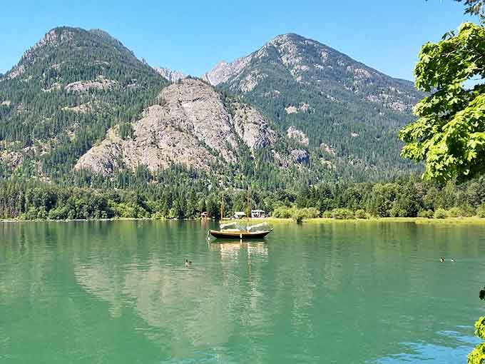 Emerald waters reflect towering peaks while a lone boat drifts peacefully, accessible only by ferry in this roadless mountain paradise.