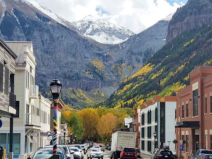 Snow-capped peaks frame this main street where fall colors paint the mountainsides in gold and green layers.