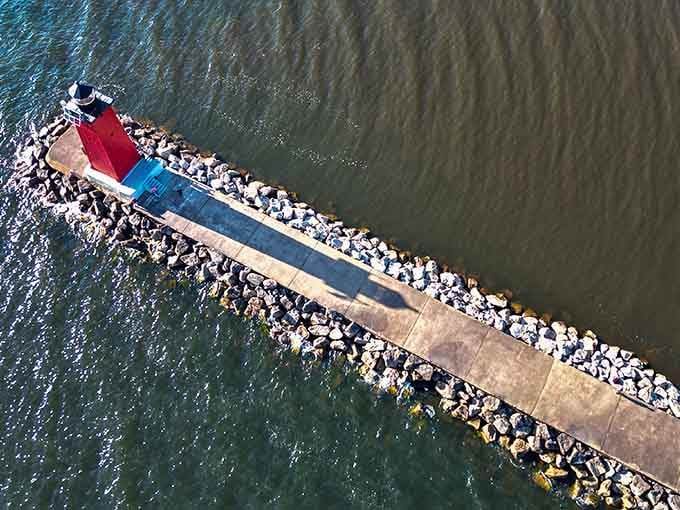 From above, the breakwater cuts through green water like a stone zipper connecting land to lighthouse.