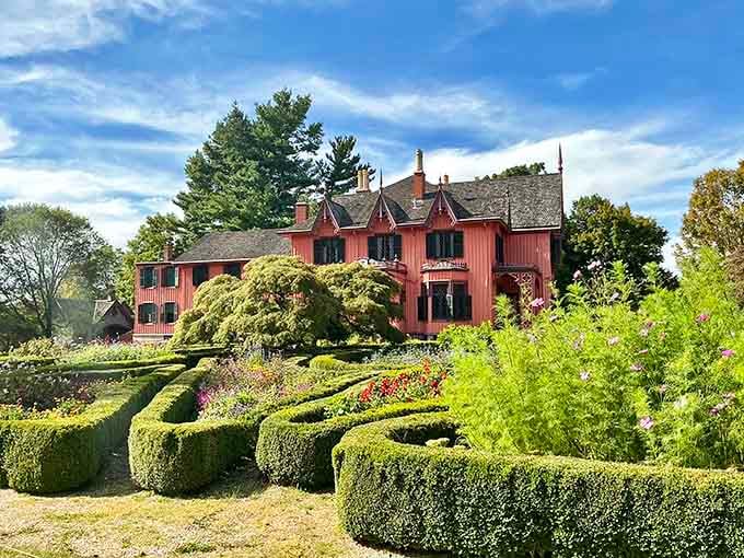 Geometric boxwood patterns frame the Gothic Revival beauty, proving that some gardens are worth every minute of meticulous trimming.