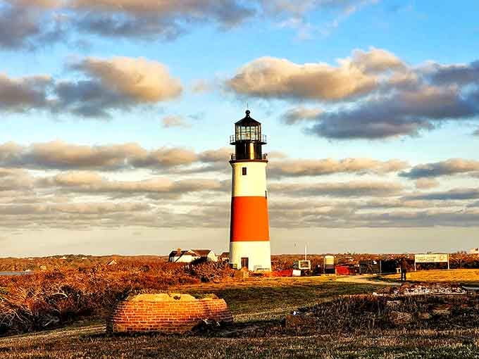 Dramatic clouds swirl above as golden light bathes the striped tower, creating an unforgettable coastal moment.