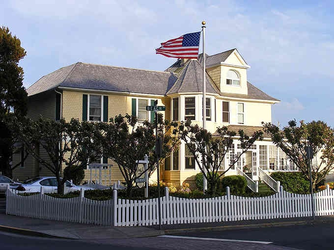 This butter-yellow Victorian house with white picket fence looks like it escaped from a Hallmark movie set.