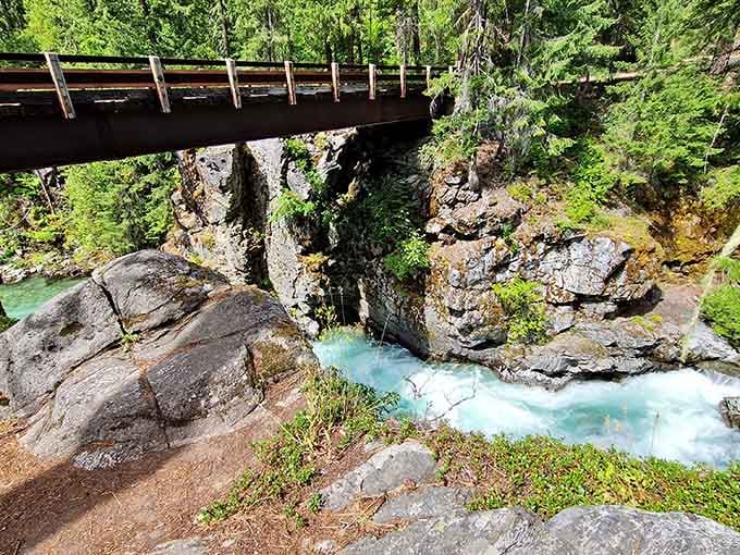 Rushing glacial water carves through ancient rock beneath a weathered bridge, painting the canyon in shades of impossible turquoise blue.