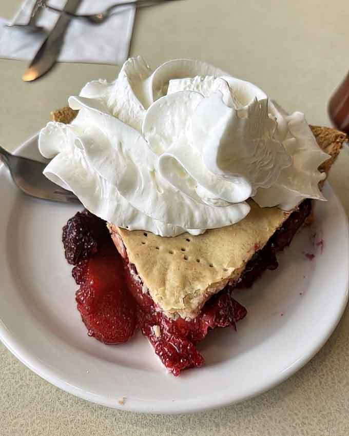 Fruit pie topped with whipped cream so generous it looks like a fluffy cloud decided to vacation here.