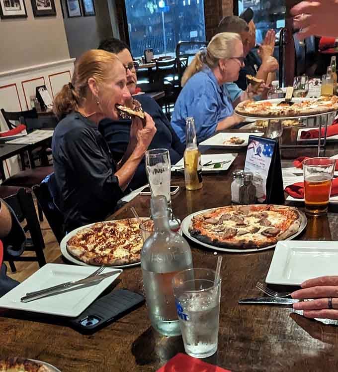 Nothing captures pure joy quite like someone mid-bite, surrounded by friends and oversized pizza pies.