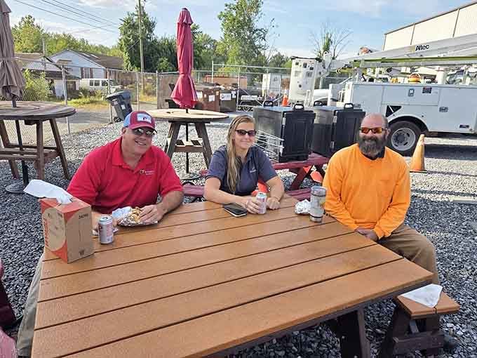 Three happy diners enjoying their feast at picnic tables, living their best barbecue life on a sunny afternoon.