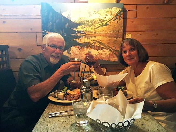 Happy diners toast their wine glasses beneath a stunning Colorado landscape photo, celebrating good food and great company.