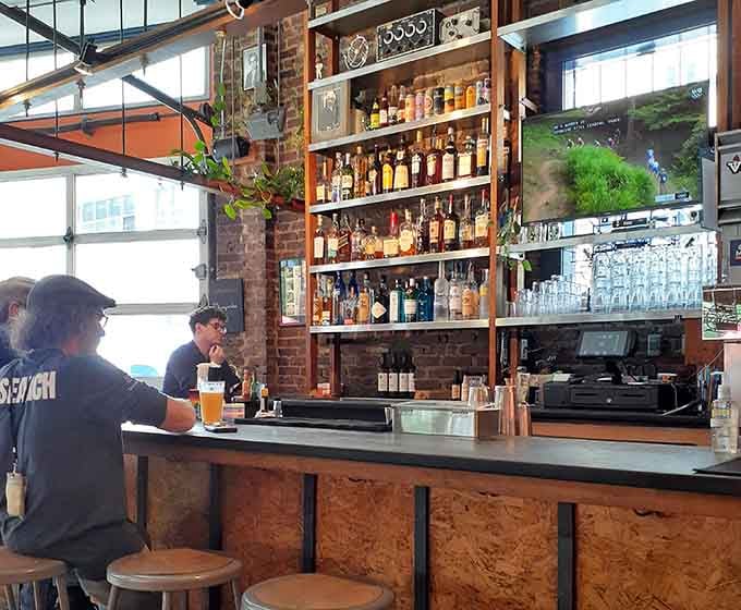 Exposed brick, gleaming bottles, and warm wood create a bar backdrop that invites you to settle in for the long haul.