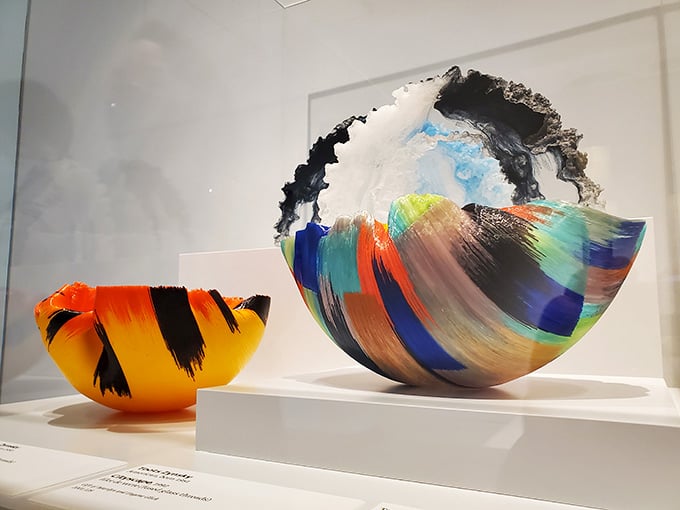 Hand-blown glass vessels burst with color like frozen fireworks captured mid-explosion on a pristine white shelf.