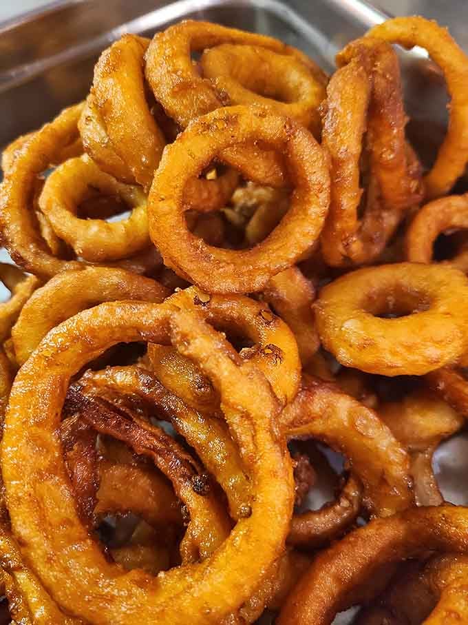 Golden onion rings stacked high, crispy and perfect, proving that vegetables can be delicious when properly disguised.