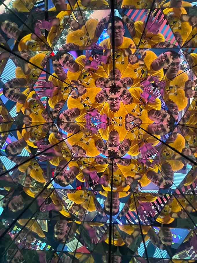 The kaleidoscope room where one yellow shirt becomes an entire sunflower made of confused, multiplied humans.