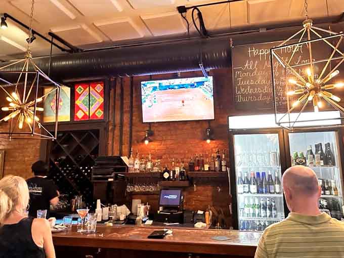 The bar area features geometric light fixtures and enough bottles to keep your evening interesting beyond just dinner.