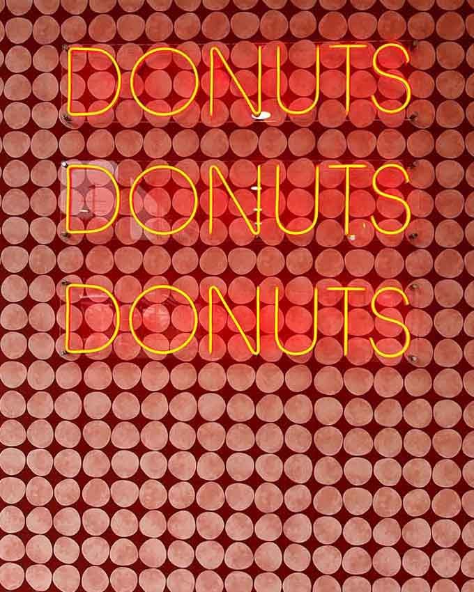 Neon signs declaring "DONUTS DONUTS DONUTS" speak the truth three times for maximum emphasis and accuracy.