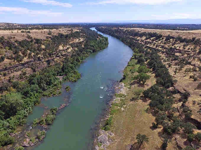 The Sacramento River carves through golden hills like nature's own highway, peaceful and timeless from above.