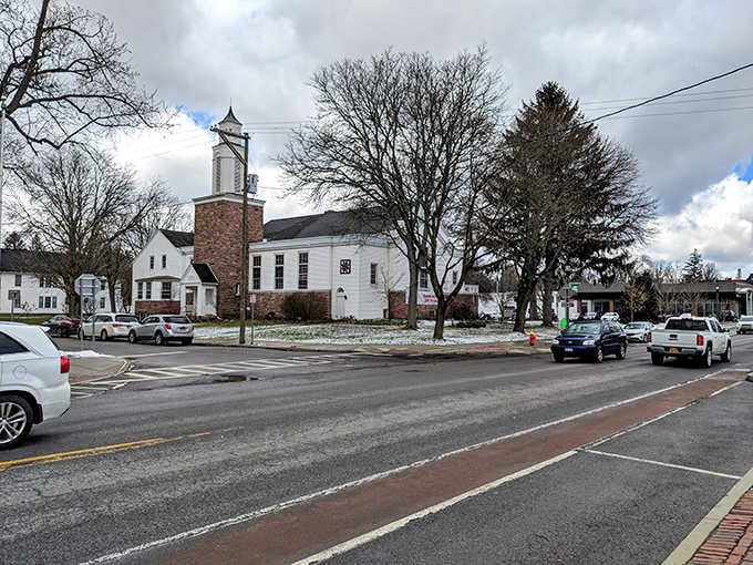 Simple white buildings and bare trees create a winter scene that feels honest, unpretentious, and wonderfully real.