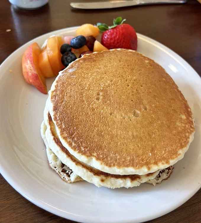 Pancakes stacked thick enough to require structural engineering, served with fruit for nutritional balance or something.