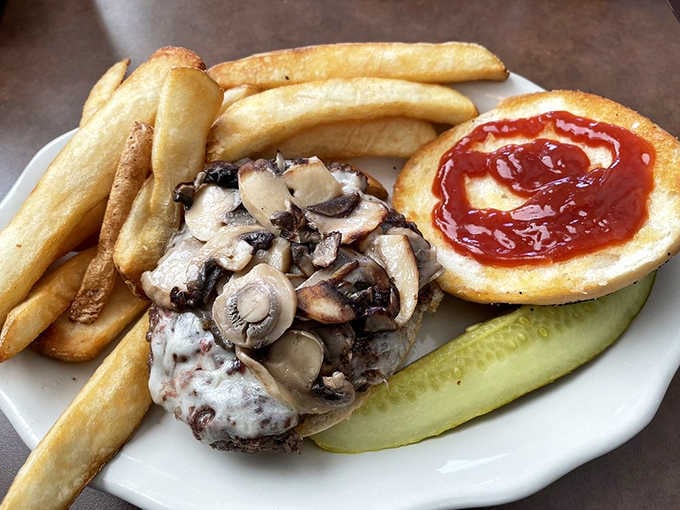 A mushroom-topped burger with fries and a pickle spear, proving that simple done right beats fancy done wrong every single time.