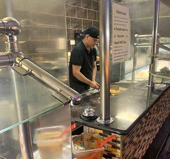 The hibachi chef working magic behind protective glass, creating sizzling masterpieces while you wait with barely contained anticipation and hunger.