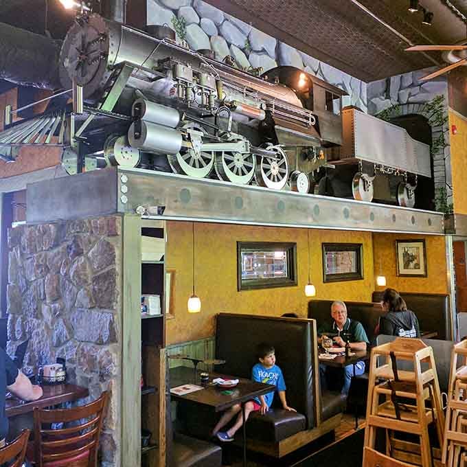 Booth seating beneath that magnificent train display creates cozy spots perfect for families or friends sharing oversized pizzas together.