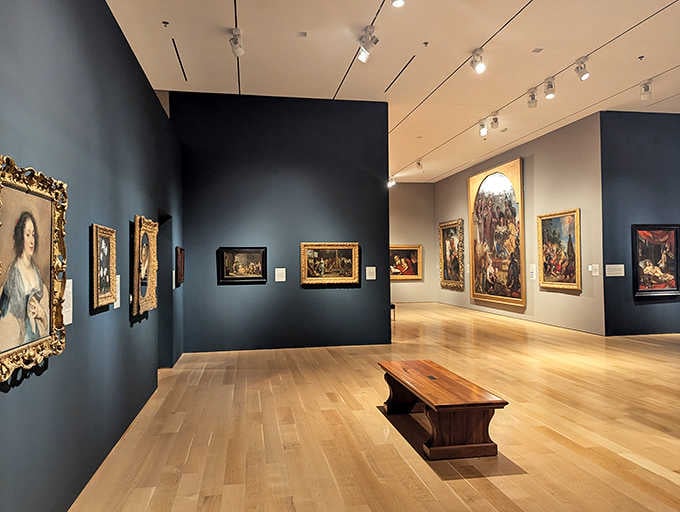 Old Master paintings glow against deep blue walls, their gilded frames catching light like precious treasure on display.