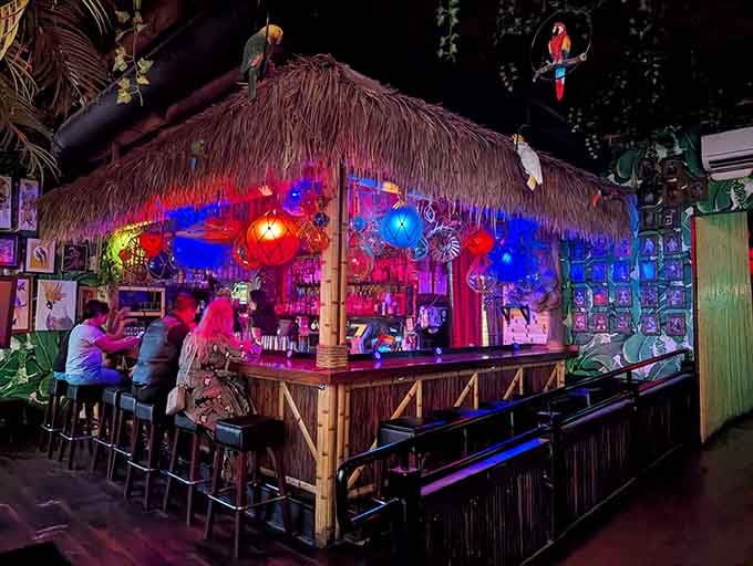 The thatched-roof bar glows with colorful lights, making every bartender look like a tropical drink wizard.