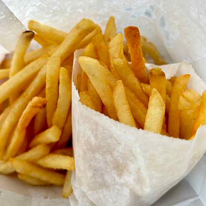 Golden fries spilling from their paper wrapper like edible treasure, crispy and perfectly salted for maximum happiness.