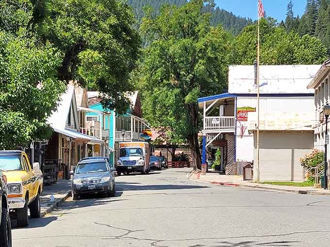 Mountain greenery surrounds these colorful storefronts where vintage trucks and modern cars share space on this peaceful small-town street.