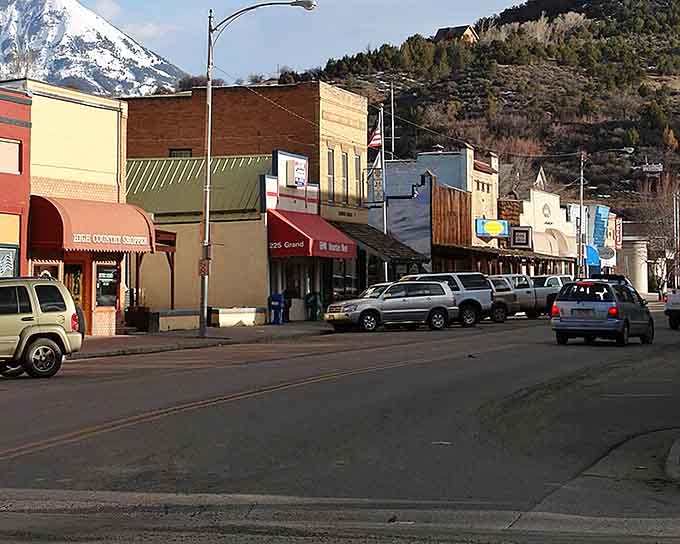 Snow-capped peaks loom behind storefronts where corrugated metal meets painted wood in rustic mountain style.