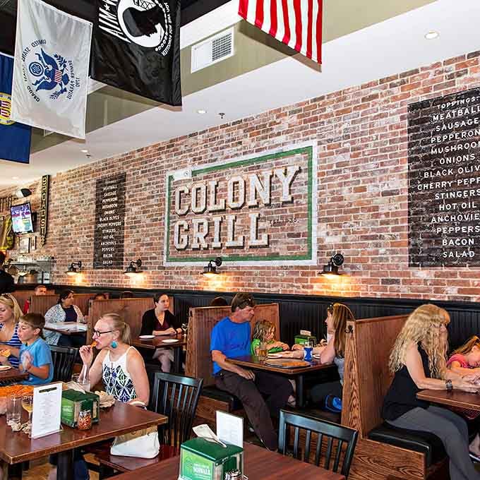 Families fill booths beneath the Colony Grill sign, proving great pizza brings generations together for dinner.