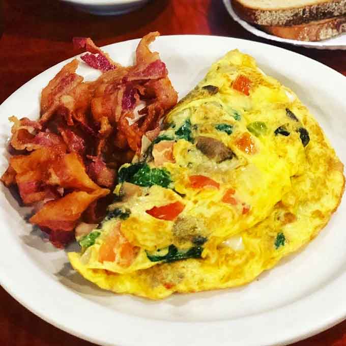 That fluffy omelet practically glows with fresh vegetables and melted cheese, accompanied by perfectly crispy bacon that knows its job.