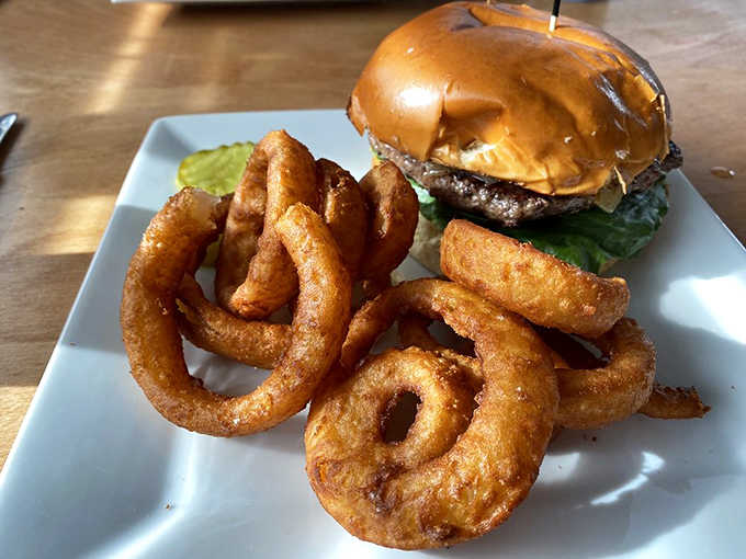 Thick onion rings tower beside a juicy burger, creating the kind of plate that makes diets take vacation days.