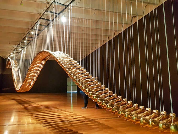 Suspended golden waves that seem to defy gravity while creating shadows that dance across the floor.
