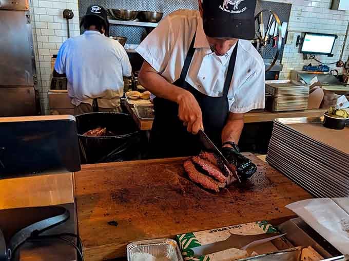 Skilled hands slice through perfectly smoked brisket at the prep station where magic transforms into plated perfection.