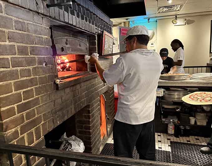 Watch the pizzaiolo slide another masterpiece into the blazing oven with practiced precision and confidence.
