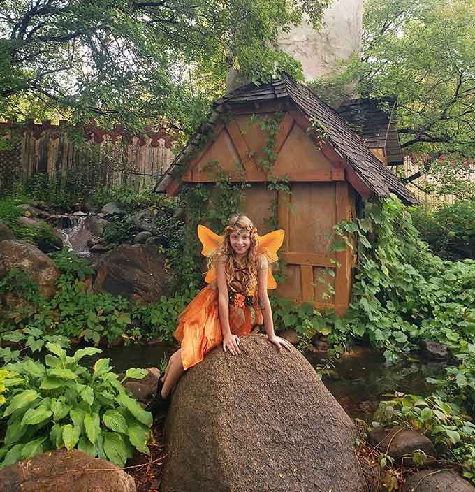 A woodland fairy poses beside her cottage, bringing storybook fantasies to life for enchanted visitors.
