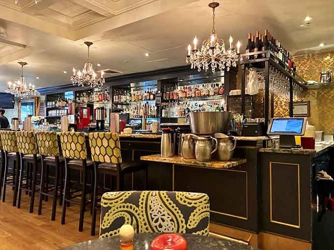 The bar area gleams with bottles and chandeliers, ready to mix brunch cocktails that justify day drinking perfectly.