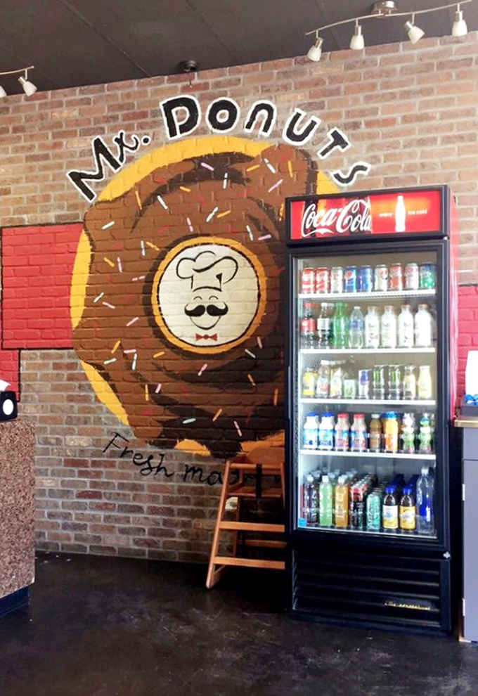 The Mr. Donuts mascot painted on brick watches over the beverage station like a delicious, mustachioed guardian angel of carbs.