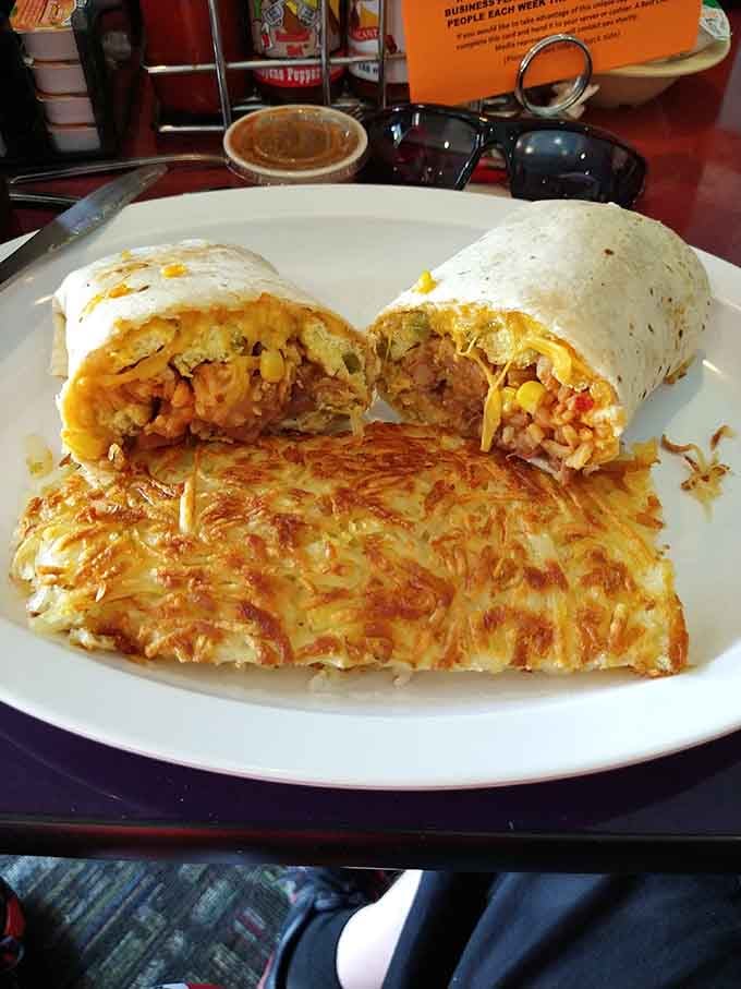 Breakfast burrito sliced open shows eggs, cheese, and filling spilling out next to crispy hash browns that could win awards for texture.