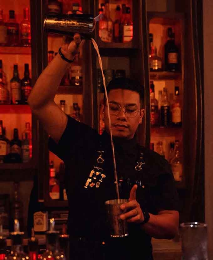 Skilled bartenders craft each drink with precision and flair, turning mixology into performance art under crimson light.