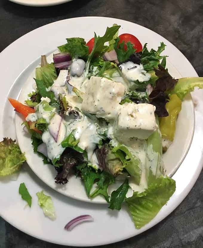 Greek salad topped with feta chunks and creamy dressing, because even diners know vegetables deserve their moment to shine.