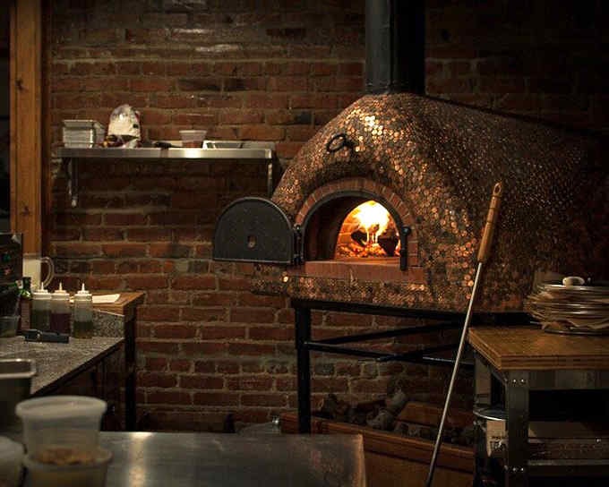 That gorgeous wood-fired oven with its glowing interior is where ordinary ingredients transform into extraordinary pizza.