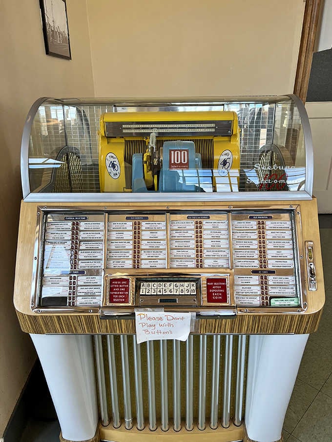 A vintage jukebox stands ready with a polite request not to play with buttons, preserving history one song selection.