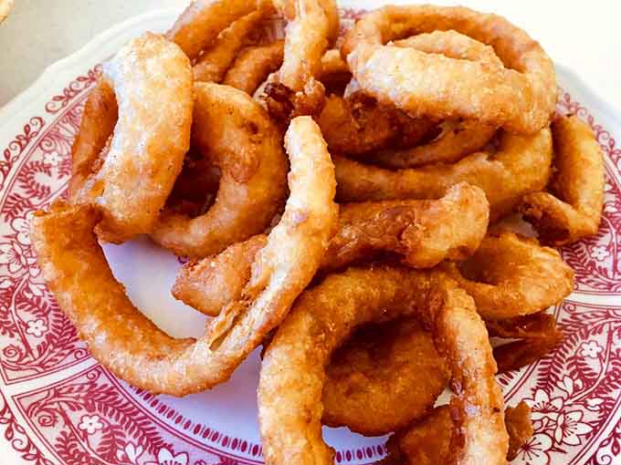 Onion rings fried to crispy golden perfection, piled high like edible jewelry on that classic diner plate.