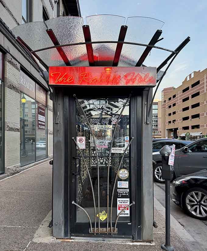Red neon glows invitingly above this underground speakeasy entrance where cocktails and curiosity lead you down the rabbit hole.