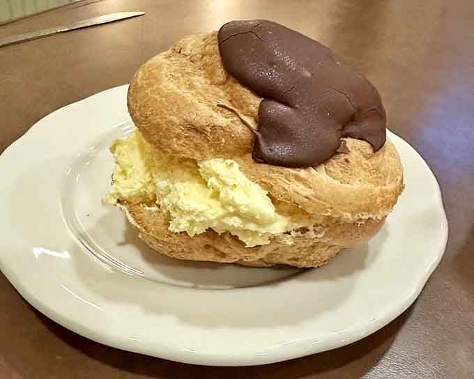 Cream puff stuffed with filling and topped with chocolate, defying gravity and common sense in the best way.