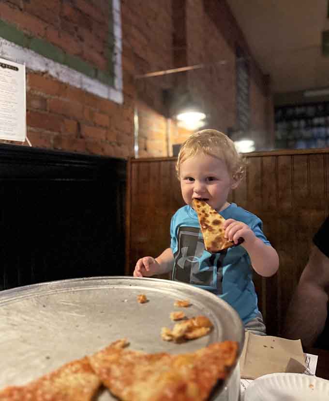 Future pizza connoisseur in training, already mastering the art of the thin-crust fold at Colony Grill.